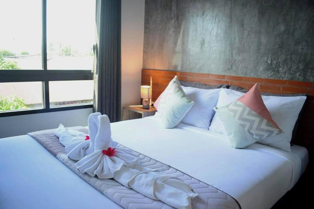Quarto de hotel com cama, almofadas, mesa de cabeceira e janela.