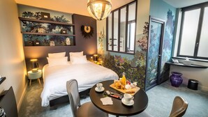 Quarto de hotel com cama, mesa redonda com itens de café da manhã, escrivaninha com computador e uma janela grande.
