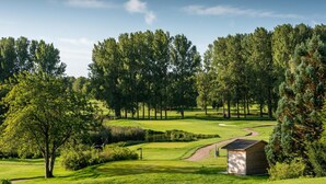 Um campo de golfe com um pequeno armazém, rodeado por árvores densas e um céu limpo.
