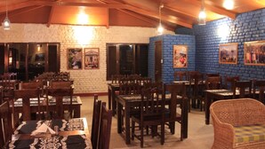 Um restaurante com mesas e cadeiras de madeira, paredes de tijolo e luminárias pendentes.