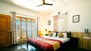 Quarto com cama, cabeceira de madeira, mesa de cabeceira, luminária, janela com cortinas e ventilador de teto.