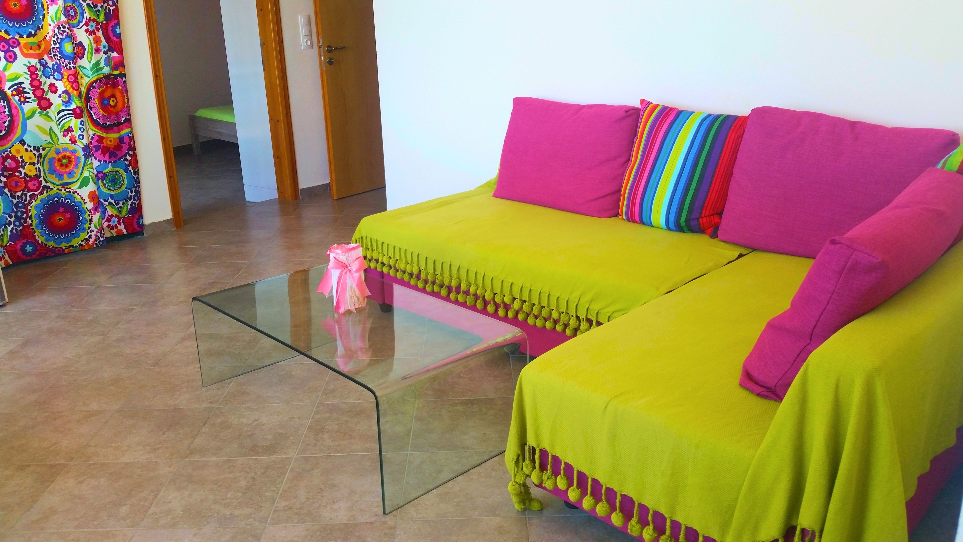 Quarto com sofá verde, almofadas cor-de-rosa e uma mesa de centro de vidro.