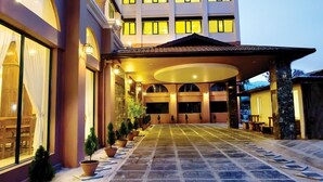 Entrada de hotel com galeria coberta, plantas em vasos e um piso de pedras.