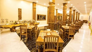 Uma sala de jantar ampla com várias mesas e cadeiras de madeira, piso de mármore e um detalhe decorativo na parede.