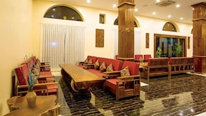 Um hall amplo com um balcão de atendimento de madeira, assentos estofados em vermelho e piso de mármore.
