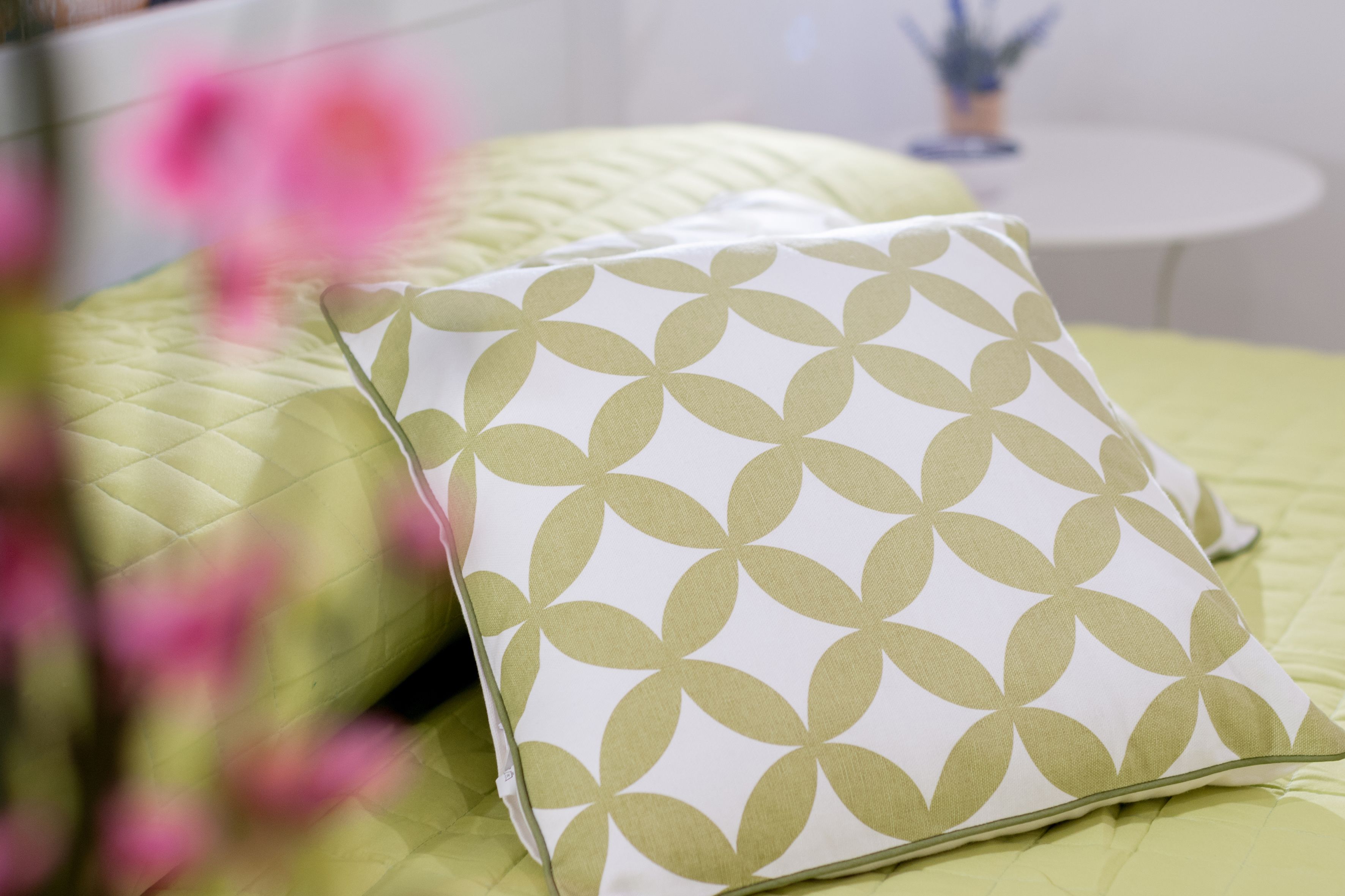 Uma cama com cobertura verde acolchoada e um travesseiro com padrão geométrico.
