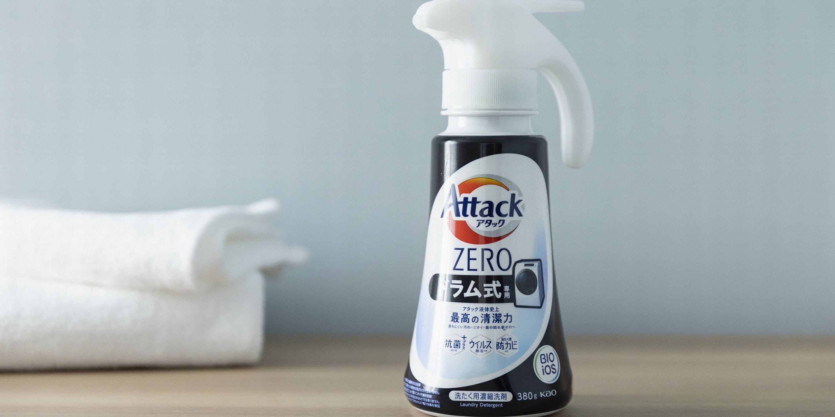 Uma embalagem de Attack Zero, detergente de lavagem, sobre uma superfície de madeira, com uma toalha branca dobrada ao fundo.