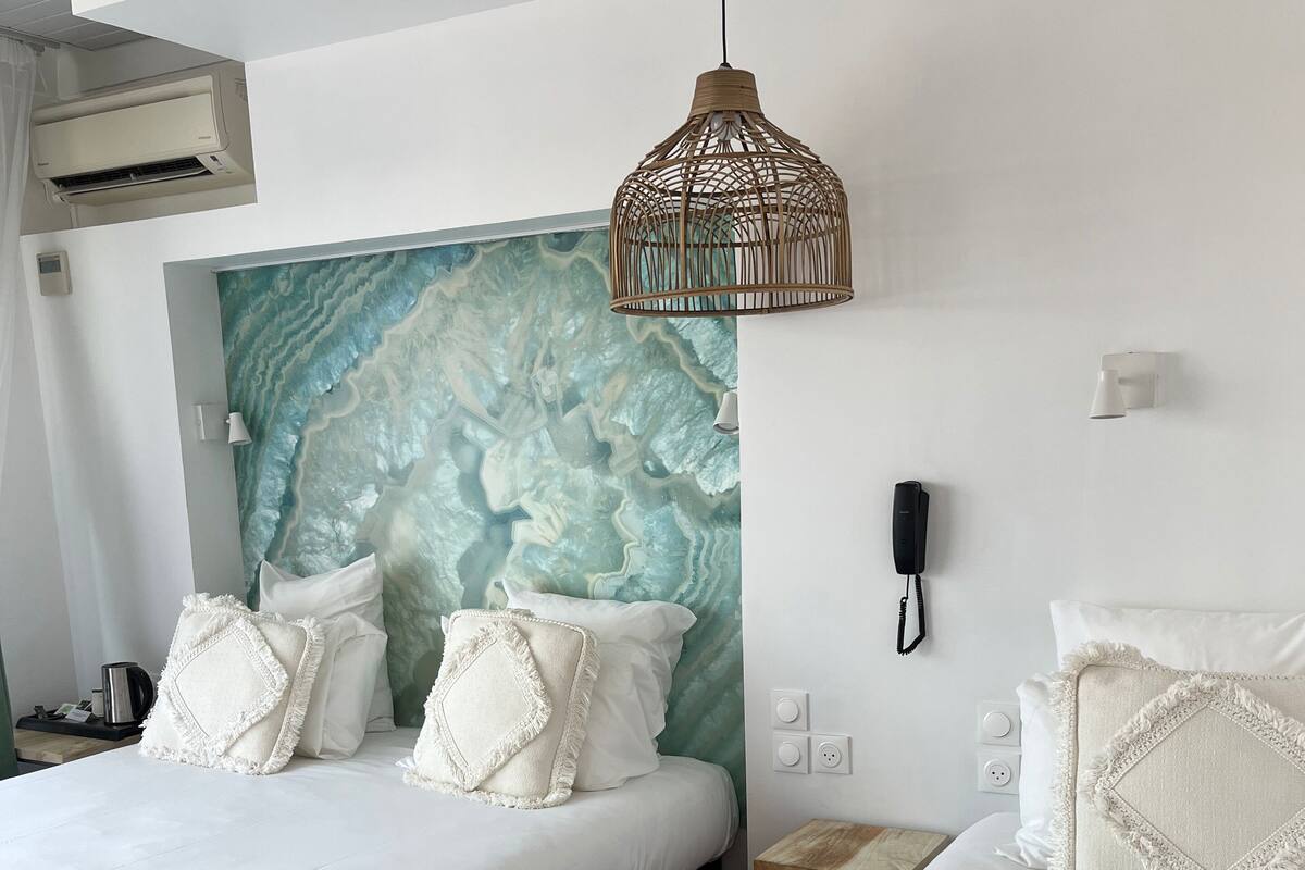 Quarto de hotel com duas camas, um grande mural abstrato na parede, um candeeiro tecido pendente e um telefone na parede.