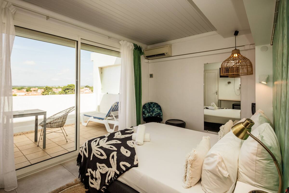 Quarto de hotel com cama, escrivaninha, cadeira, varanda e vista para a paisagem.