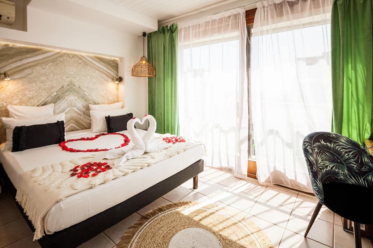 Uma cama bem arrumada com uma decoração em formato de coração, um tapete tecido e uma cadeira.