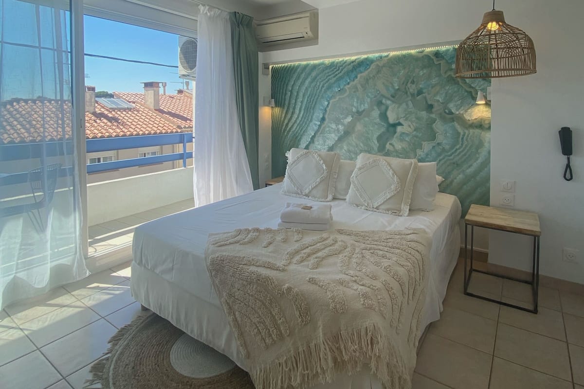 Quarto com cama, mesa de cabeceira, telefone fixado na parede e vista para o exterior.