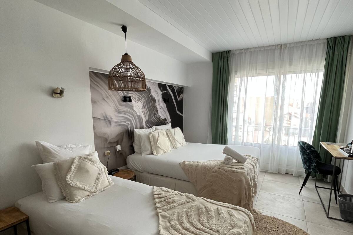 Quarto de hotel moderno com duas camas, uma grande pintura abstrata na parede, um tapete tecido e uma escrivaninha com uma cadeira.