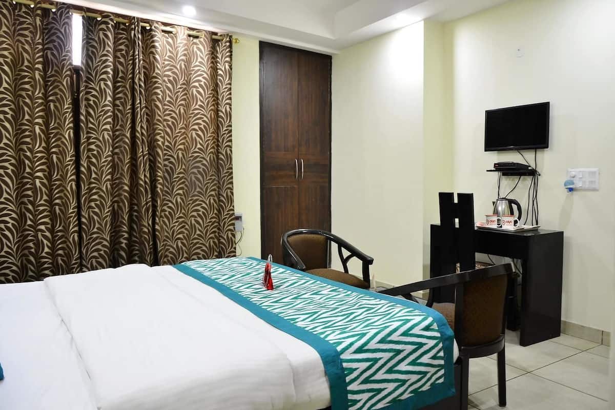 Quarto de hotel com uma cama, escrivaninha, cadeira, televisão e guarda-roupa.