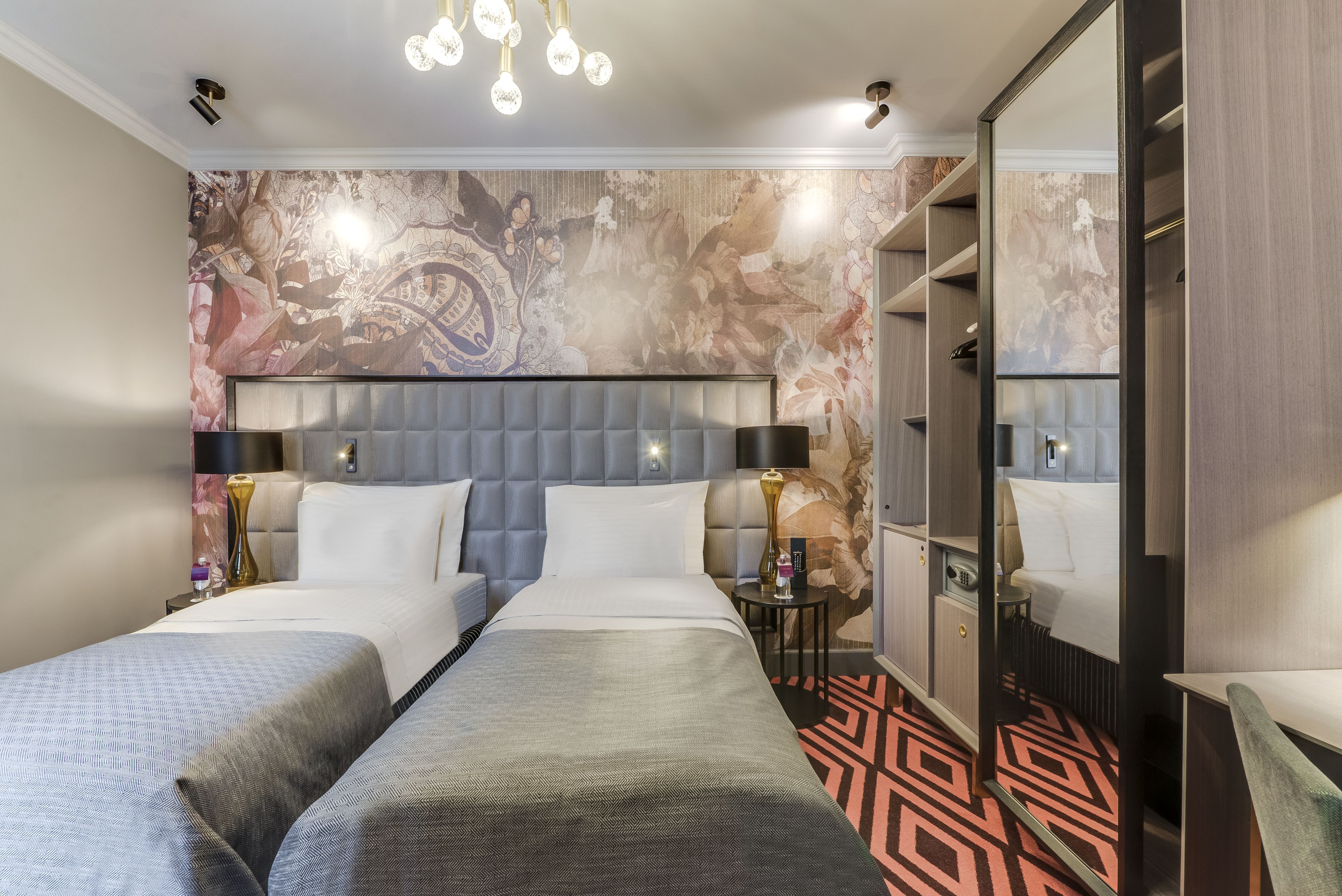 Quarto de hotel com uma cama grande, duas mesas de cabeceira, um guarda-roupa e um espelho.