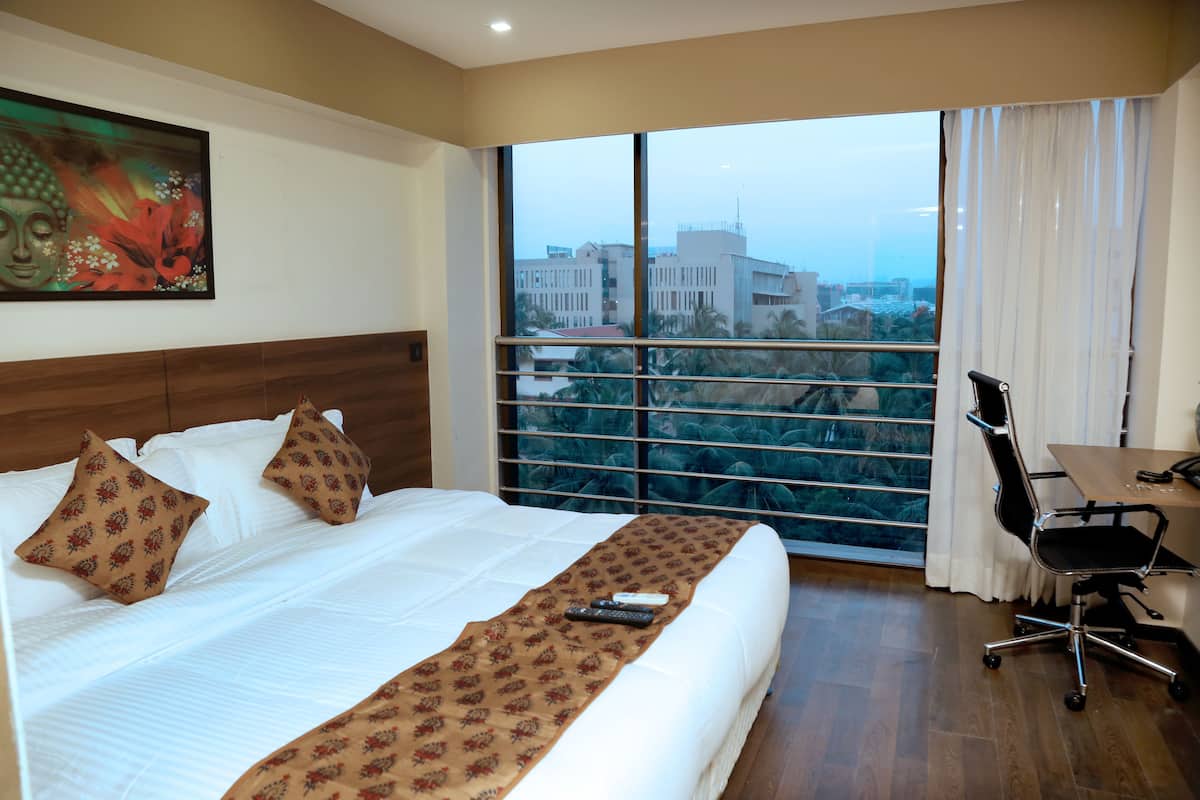 Quarto de hotel com uma cama grande, uma escrivaninha e vista da cidade através de uma janela ampla.