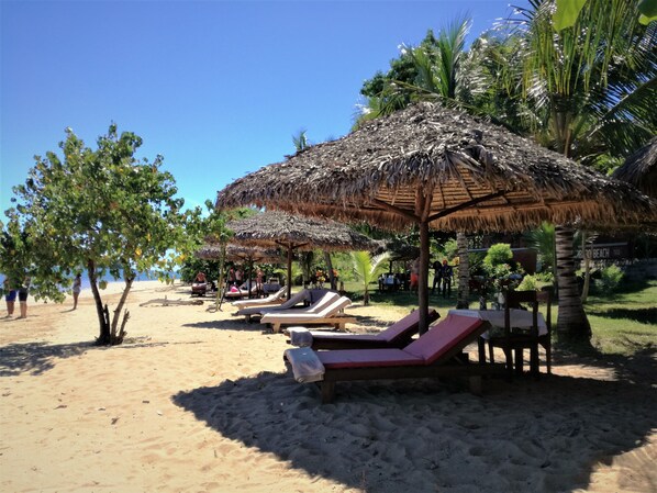 Uma praia com palafitas, cadeiras de praia e palmeiras.