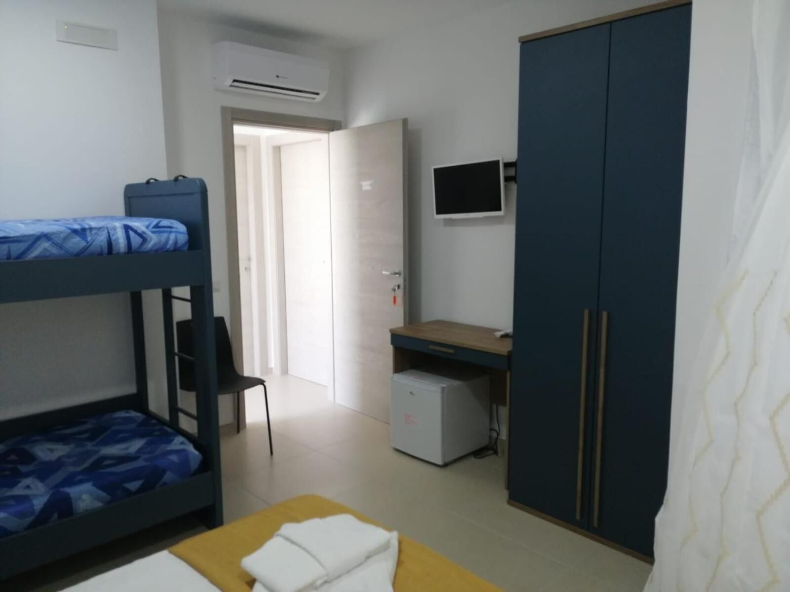 Quarto de dormitório com beliches, escrivaninha, cadeira, televisão e guarda-roupa.