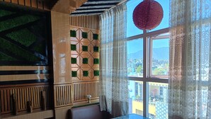 Quarto com divisória de madeira, mesa de vidro e vista para edifícios pela janela.