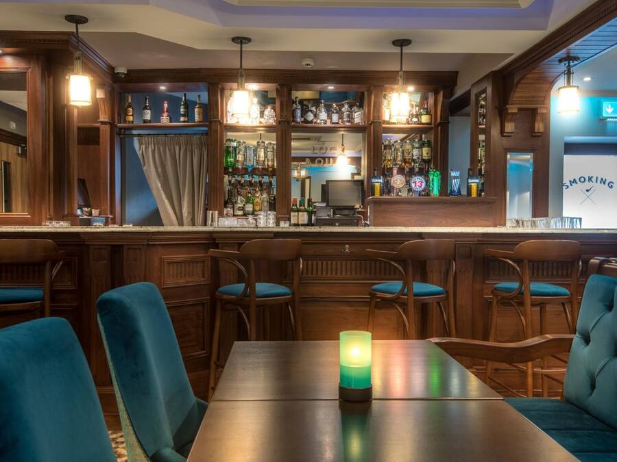 Uma área de bar com mobiliário de madeira, um balcão com garrafas e uma mesa com uma vela.