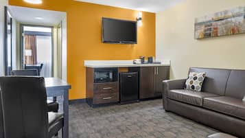 Quarto de hotel moderno com cozinha compacta, televisão de tela plana, sofá de couro marrom e carpete estampado.