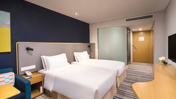 Quarto de hotel com duas camas, uma escrivaninha, uma cadeira e uma televisão.
