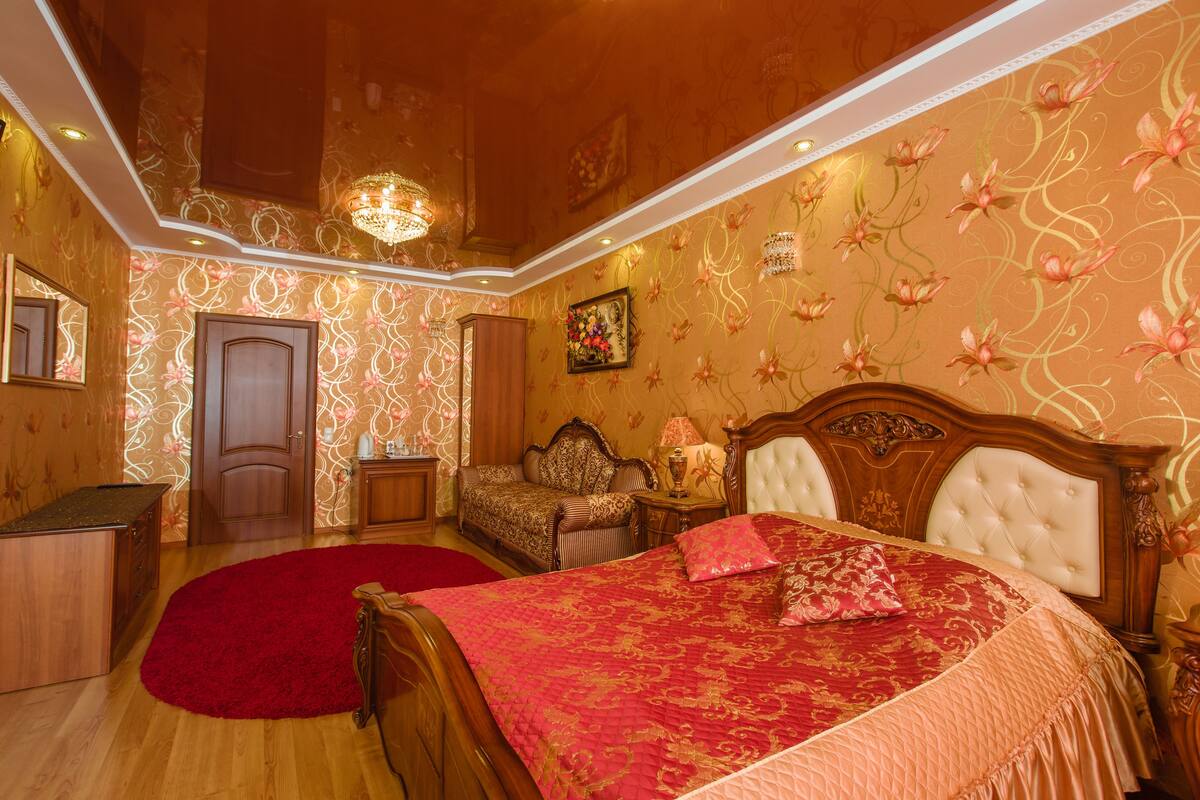 Um quarto com uma cama grande, cômoda de madeira, mesa de cabeceira e tapete vermelho.