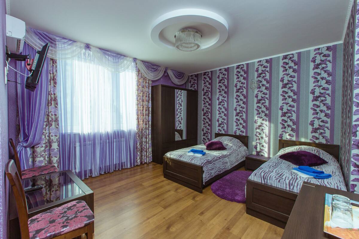 Quarto com duas camas, uma mesa de vidro e cortinas roxas.