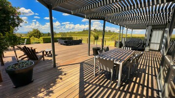 Um deck de madeira com móveis de exterior, uma pérgula e vista para uma paisagem verde.