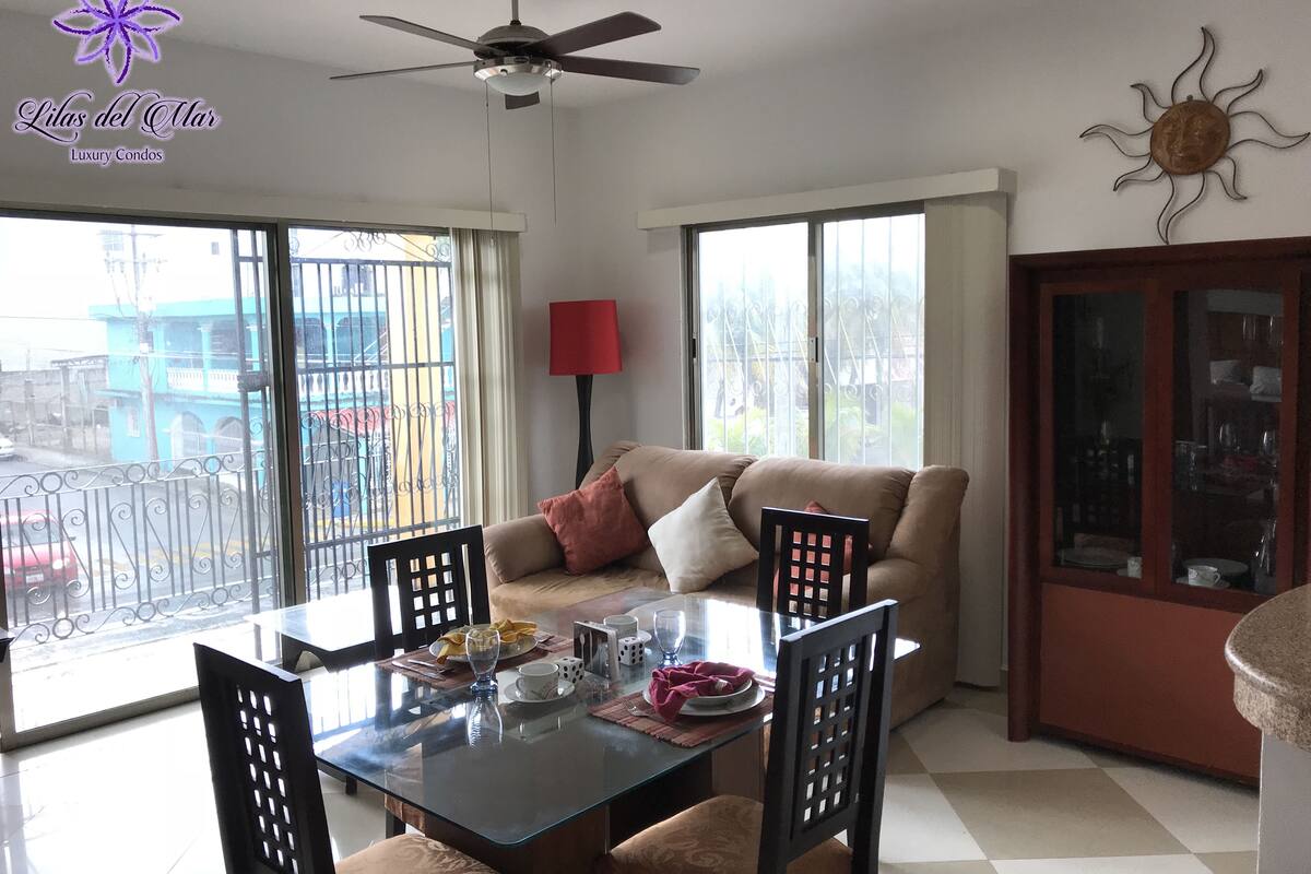 Uma sala de estar espaçosa com mesa de jantar de vidro, assentos confortáveis e grandes janelas com vista para a rua.