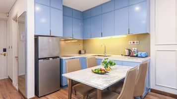 Uma cozinha compacta com armários azuis, geladeira de aço inoxidável, bancada de mármore e uma mesa de jantar com cadeiras.