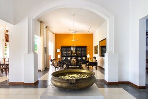 Uma sala de estar ampla com uma grande tigela decorativa no centro, um ventilador de teto e um armário preto com quadros emoldurados.