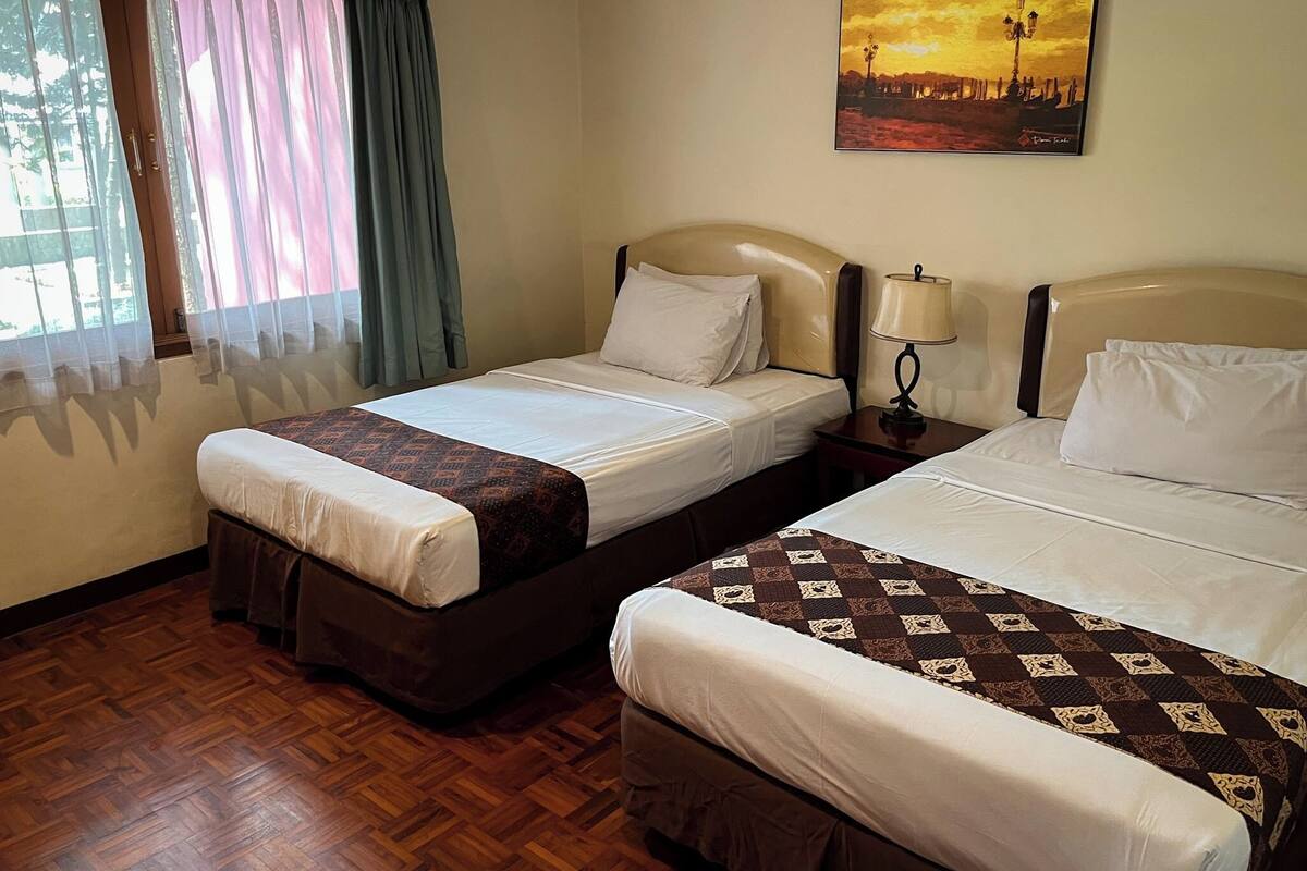 Quarto de hotel com duas camas, piso de madeira, janela com cortinas e um quadro na parede.