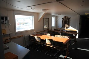 Uma sala de conferência com uma mesa grande, cadeiras, um quadro branco e uma janela com vista para um edifício.