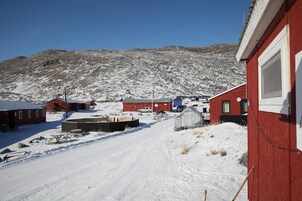 Paisagem nevada com edifícios vermelhos, céu claro e montanha ao fundo.