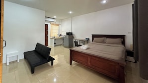 Quarto com cama, escrivaninha, cadeira e cozinha compacta.