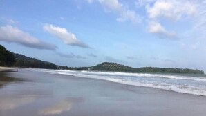 Uma praia com ondas, uma colina ao longe e céu claro.