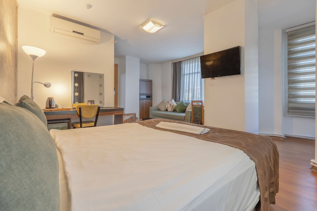 Quarto de hotel com uma cama grande, uma escrivaninha com cadeira, televisão e janela com persianas.