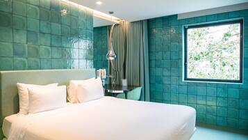 Quarto de hotel com uma cama grande, mesa de cabeceira, janela com vista para árvores e paredes cor de verde-água.