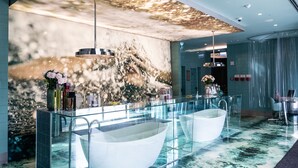 Casa de banho moderna com cabine de vidro, duas banheiras brancas e parede de mármore com design de cascata.