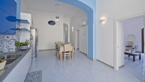 Uma sala de estar ampla com uma mesa de jantar, cadeiras e uma área de cozinha com geladeira e pia.