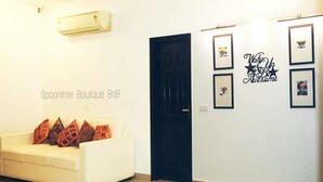 Sofá branco com almofadas estampadas em um quarto com parede branca, porta preta e obras de arte emolduradas.