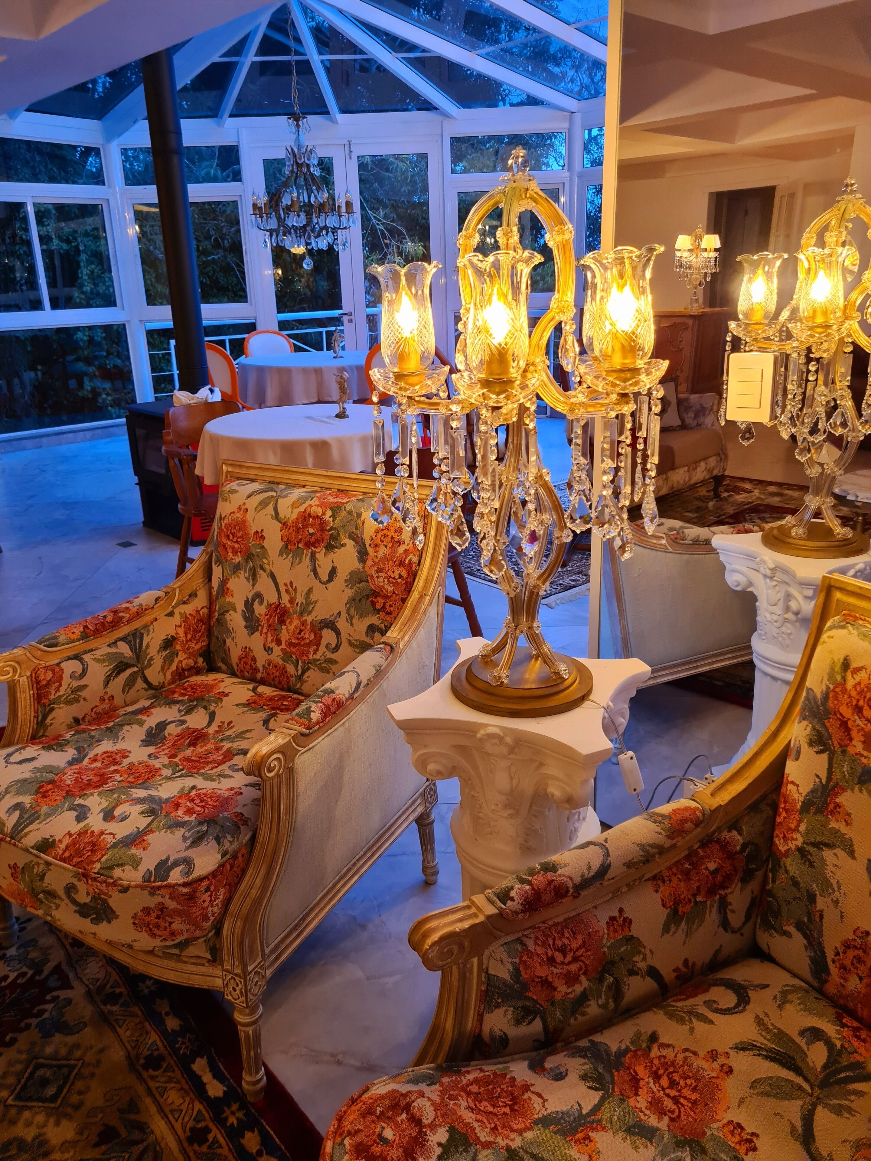 Um quarto luxuoso com poltronas estofadas com motivos florais elaborados, uma mesa branca e um lustre.
