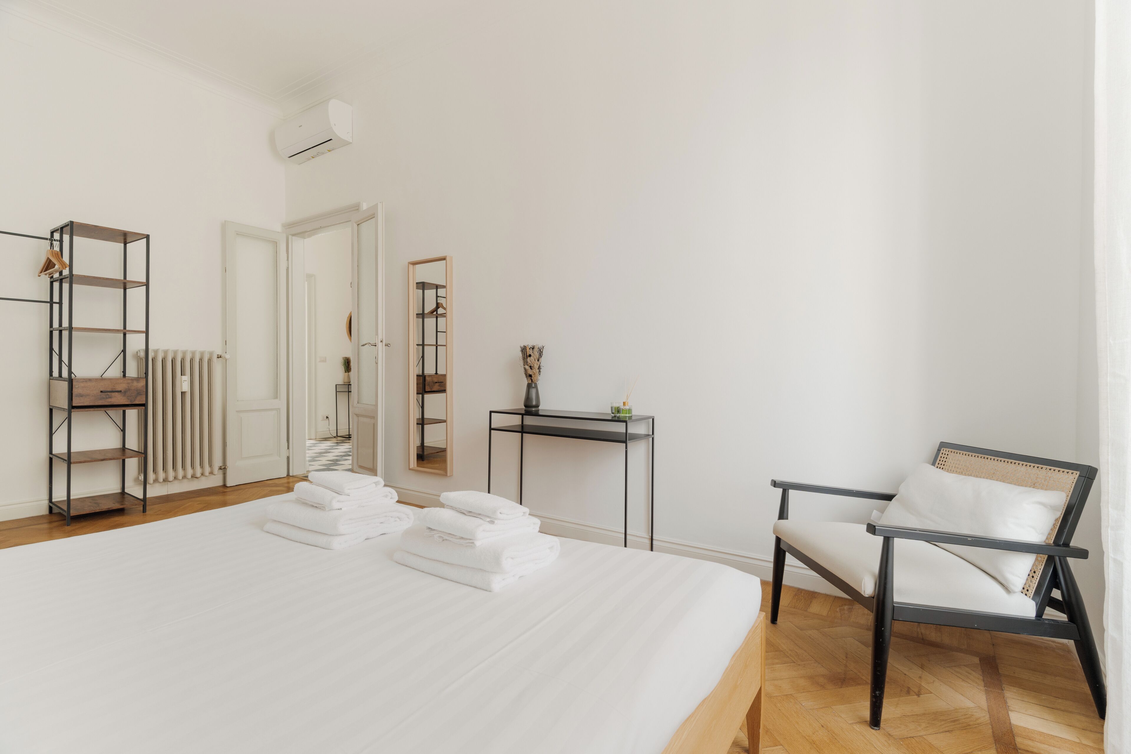 Quarto de hotel com uma cama grande, uma cadeira, uma mesa pequena e um radiador.