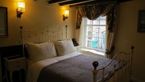 Quarto com cama, mesas de cabeceira, janela com cortinas e luminárias na parede.