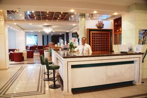 Uma área de recepção de hotel com balcão de mármore, banquetas e um lustre.