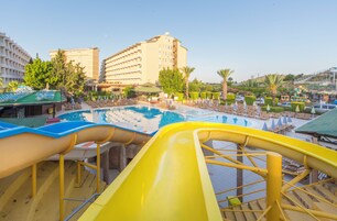 Área de piscina de hotel com vários toboáguas, céu azul e edifícios ao redor.