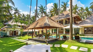 Um resort com construções de palha, piscina e vegetação exuberante.