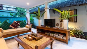 Uma sala de estar moderna com sofá, mesa de centro e aparador de TV, cercada por plantas e livros.