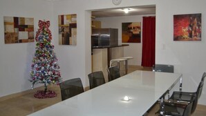 Uma sala de jantar com uma grande mesa branca, várias cadeiras, um pinheiro de Natal e obras de arte nas paredes.
