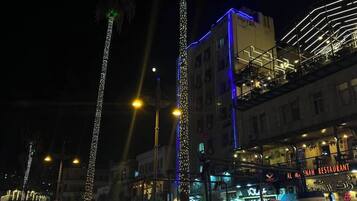 Uma rua urbana à noite, com edifícios e veículos iluminados.